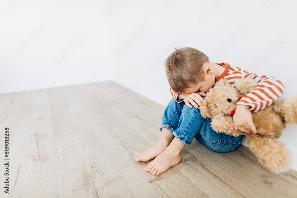 Lonely scared sad little boy with teddy bear sitting on floor in empty ...