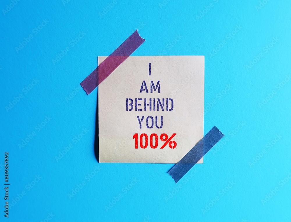 Note stck on blue background written - I am behind you 100% - means totally support someone ...