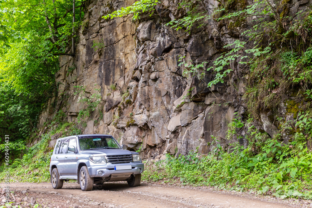 Off-road 4x4 car driving on a gravel road with vertical stone cliff ...