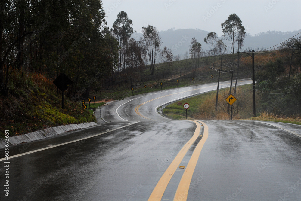 Estrada asfaltada molhada em dia de chuva, com placa indicativa de ...