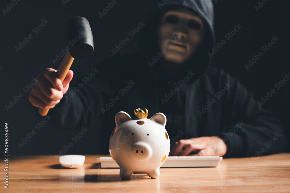 Black hat hacker in mask and hoodie trying to destroy financial piggy ...