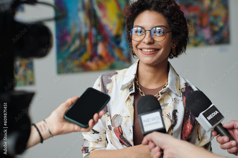 Young smiling artist giving an interview at her exhibition in art ...