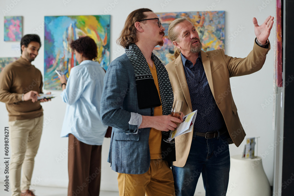 Art lovers discussing modern art in gallery, they pointing at wall with ...