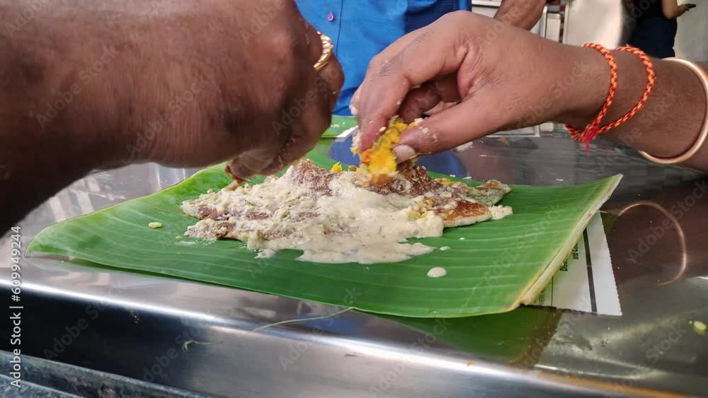 Closeup of friends sharing and eating masala dosa at a roadside hotel ...