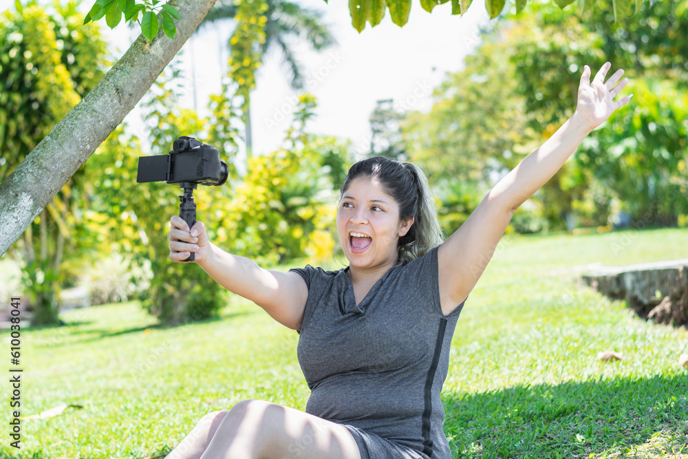 latina blogger girl sitting on the grass in the park recording a video ...