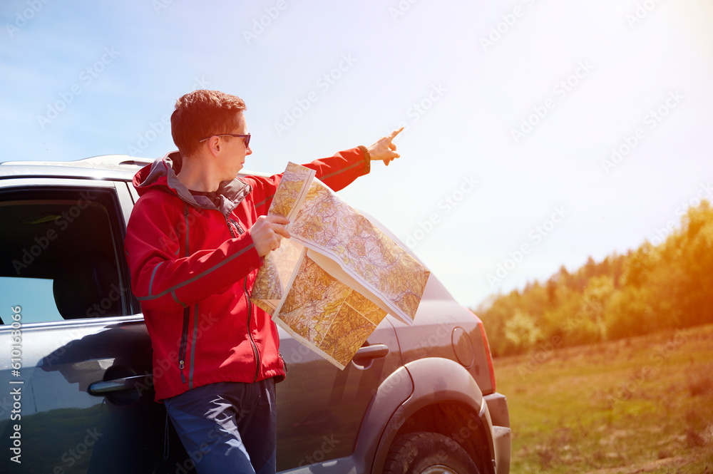 A man leans against a car, holding a map in his hands, as he looks for ...