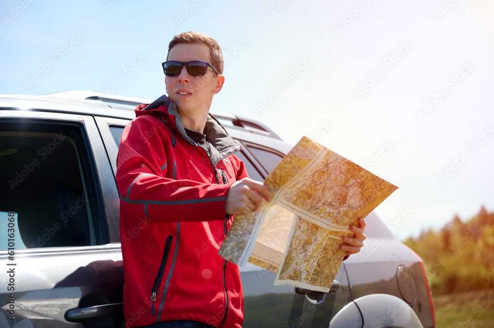 A man leans against a car, holding a map in his hands, as he looks for ...