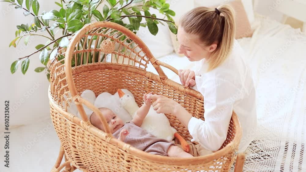 a young mother puts her little newborn baby to sleep in a wicker cradle ...