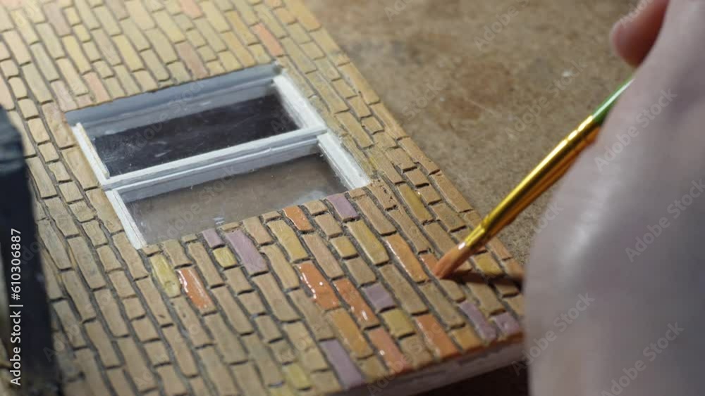 A miniature brick wall with a window is crafted by a master, who ...