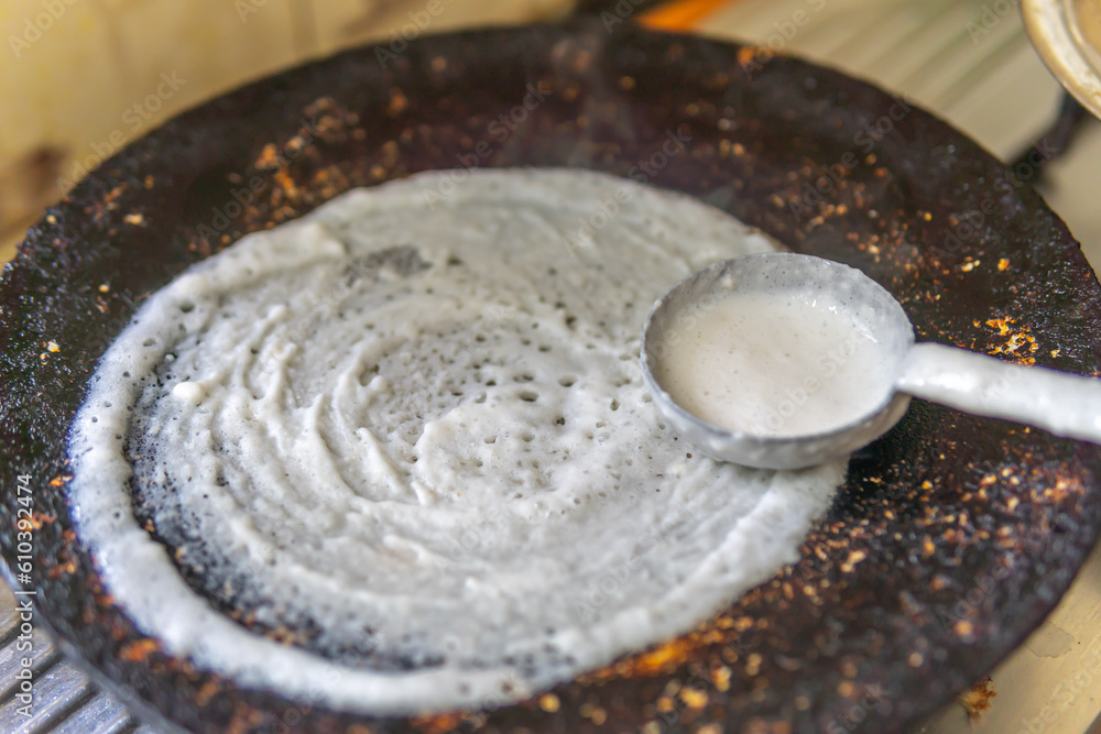 On a black dosa tawa, a skilled cook expertly spreads dosa batter with ...