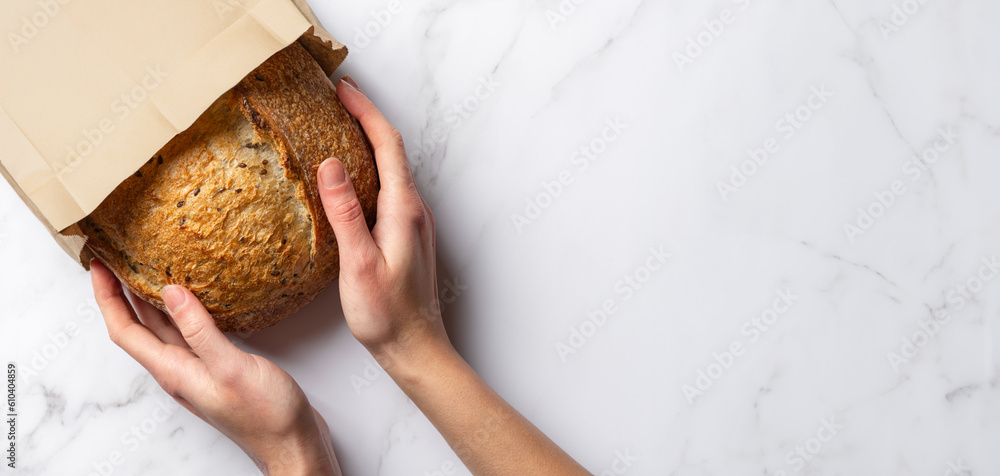 Fresh sourdough bread in woman's hands, top view. Woman takes a loaf of ...