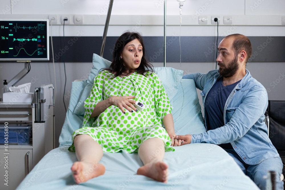Pregnant patient sitting in hospital ward bed with husband beside her ...