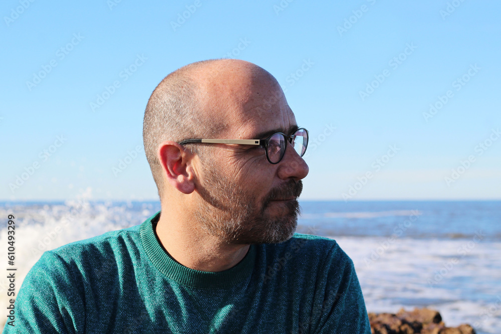 homem adulto, calvo, usando óculos e blusa verde em paisagem marítma ...
