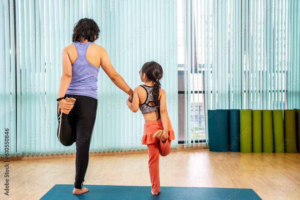 Mother and her daughter in preschool age practicing balancing yoga pose ...