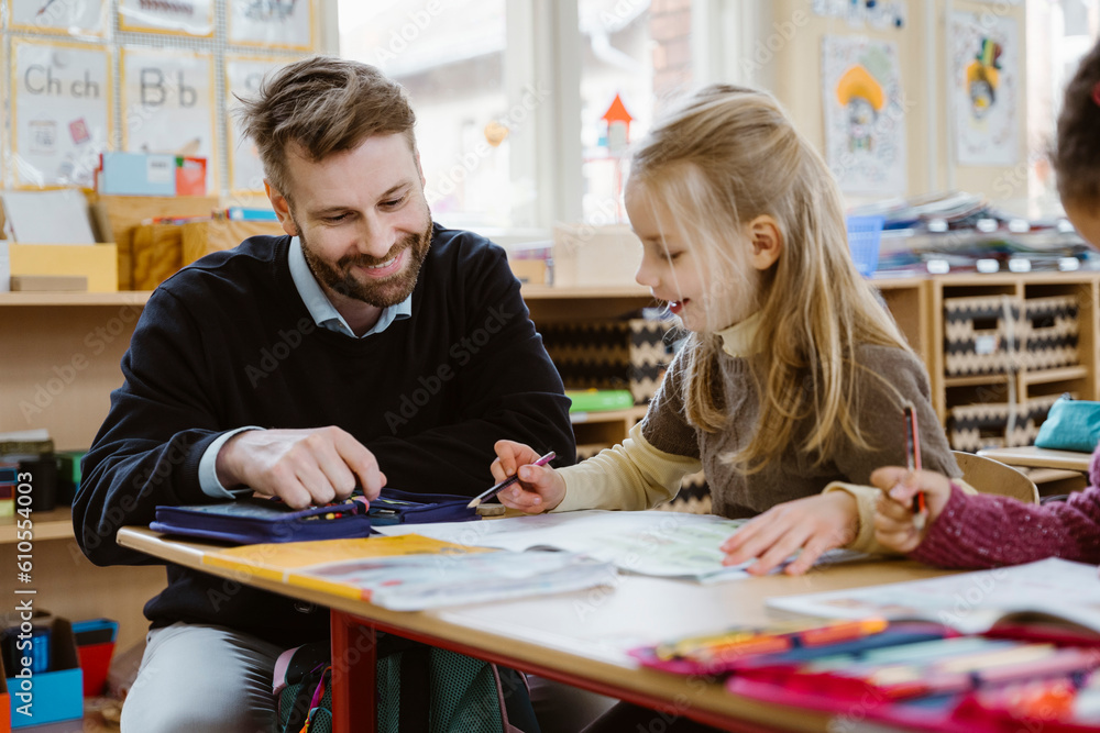 Smiling male teacher assisting female student while studying in ...
