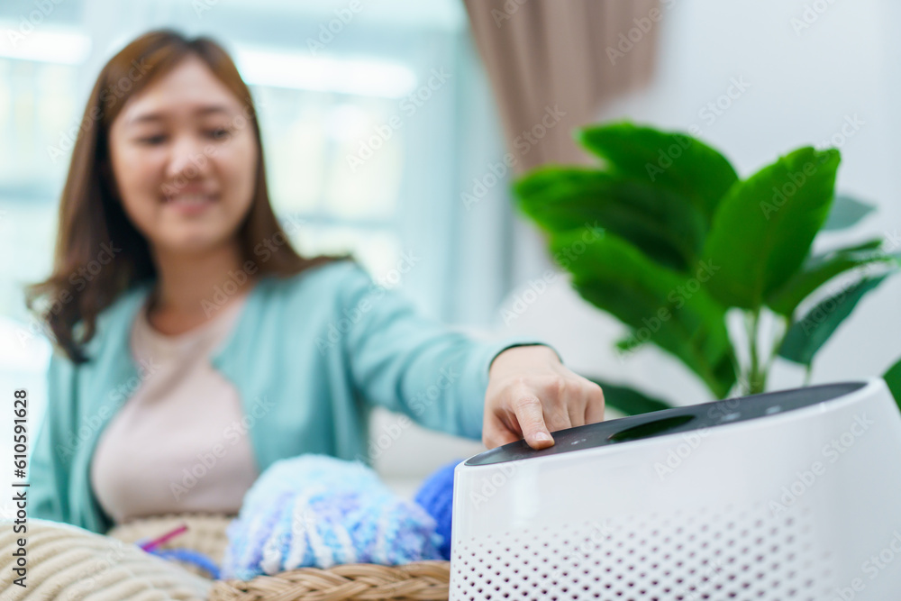 Happy Asian young woman turning on high efficiency air purifier while ...