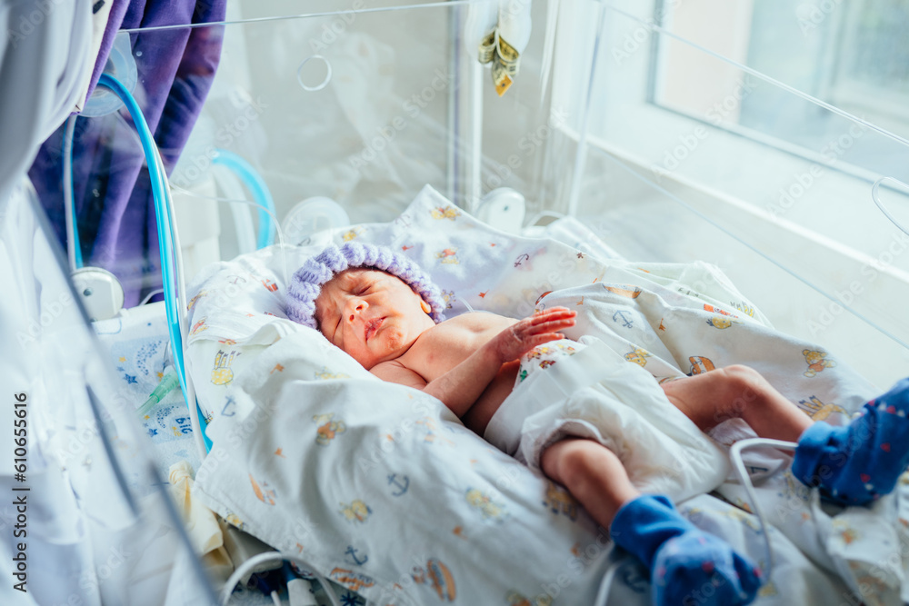 Premature newborn recovering in incubator. His foot in a blue sock with ...