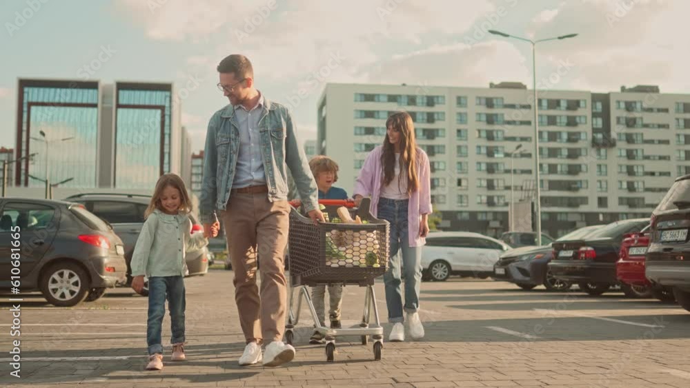 Happy family goes to car. Mother and son push cart with groceries. Dad ...