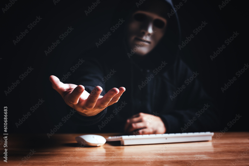 Black hood hacker force demands ransom by holding out his hand on table ...