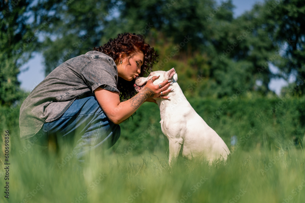 beautiful curly girl kisses the nose of a white dog of a large pit bull ...