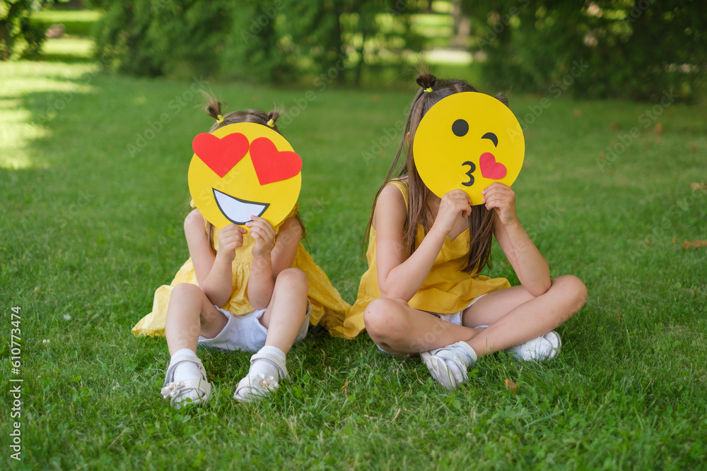 Two girls hide their faces behind the heads of emoticons with different ...
