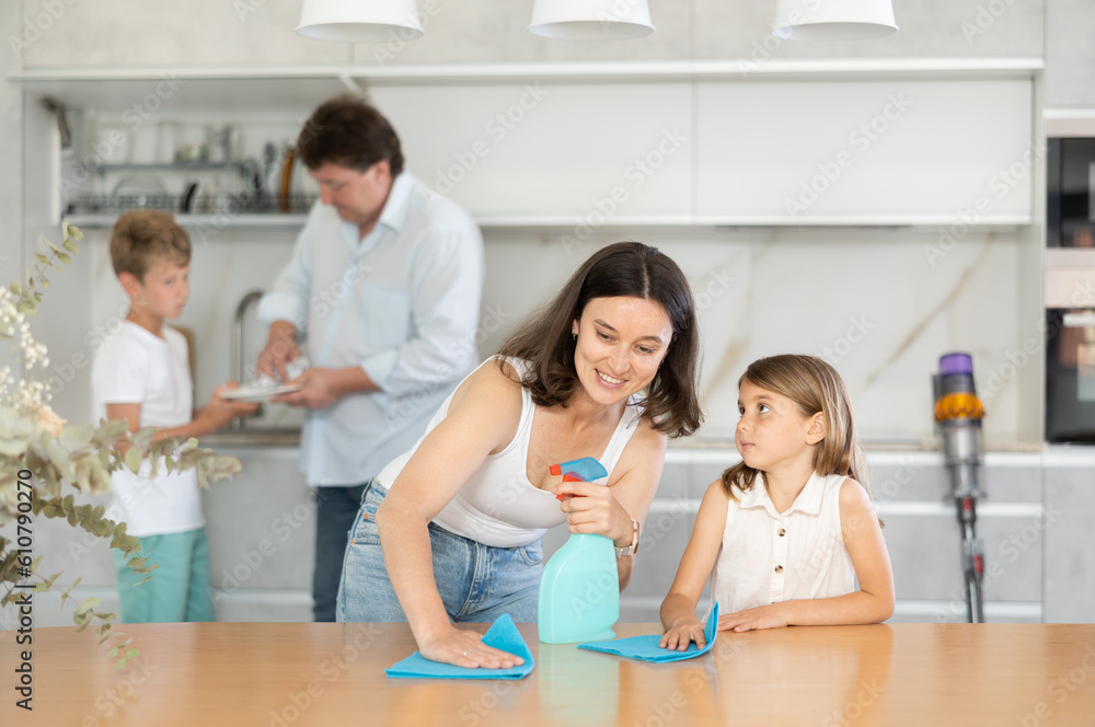 Little girl helps mother wash kitchen table. Husband and son are ...