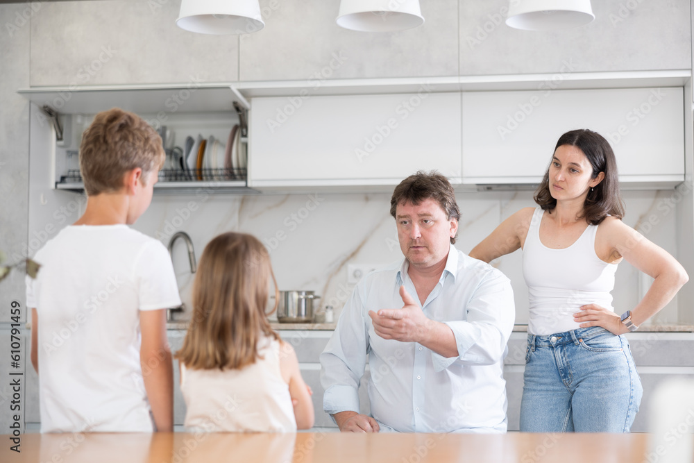Little brother and sister standing in the kitchen being admonished by ...