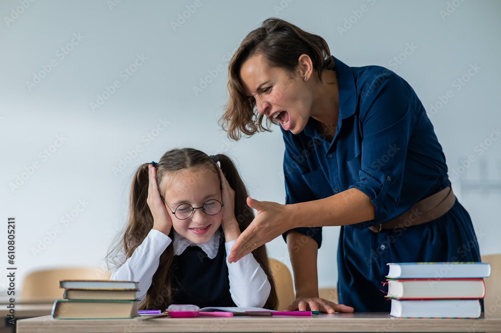 A female teacher yells at a student. Little girl covers her ears with ...