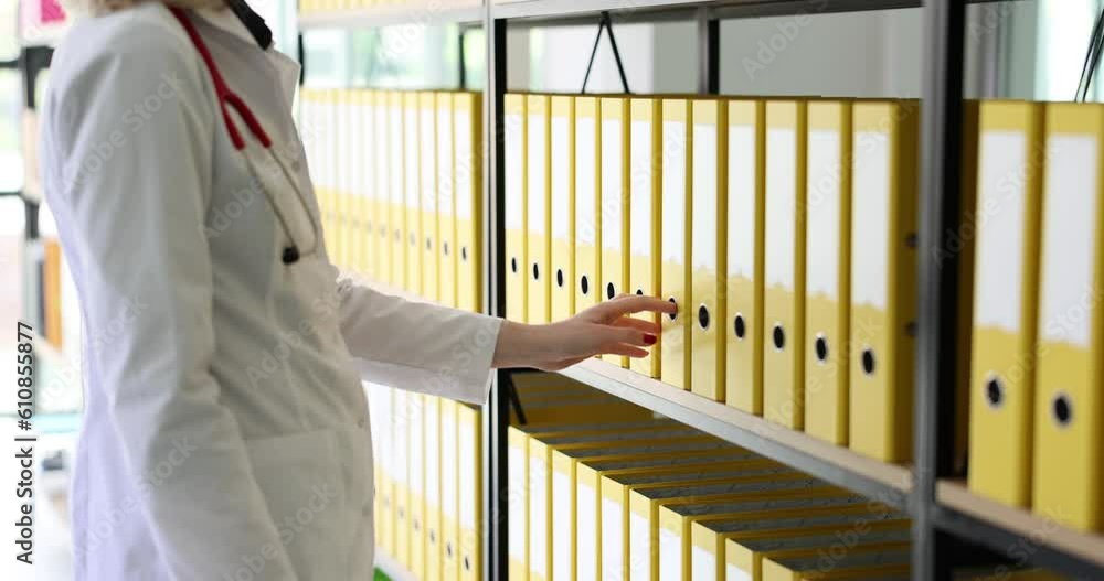 Female doctor takes yellow folder from archive from shelf. Nurse in ...