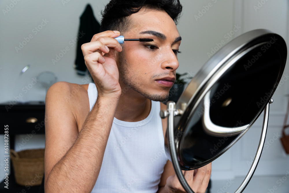 Biracial transgender man looking in mirror and putting on make-up ...