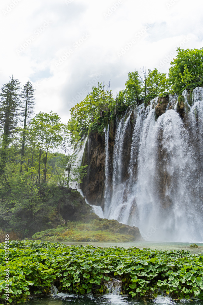 Großer Wasserfall im Nationalpark Plitvicer Seen an Felswand vor einem See mit vielen Pflanzen ...