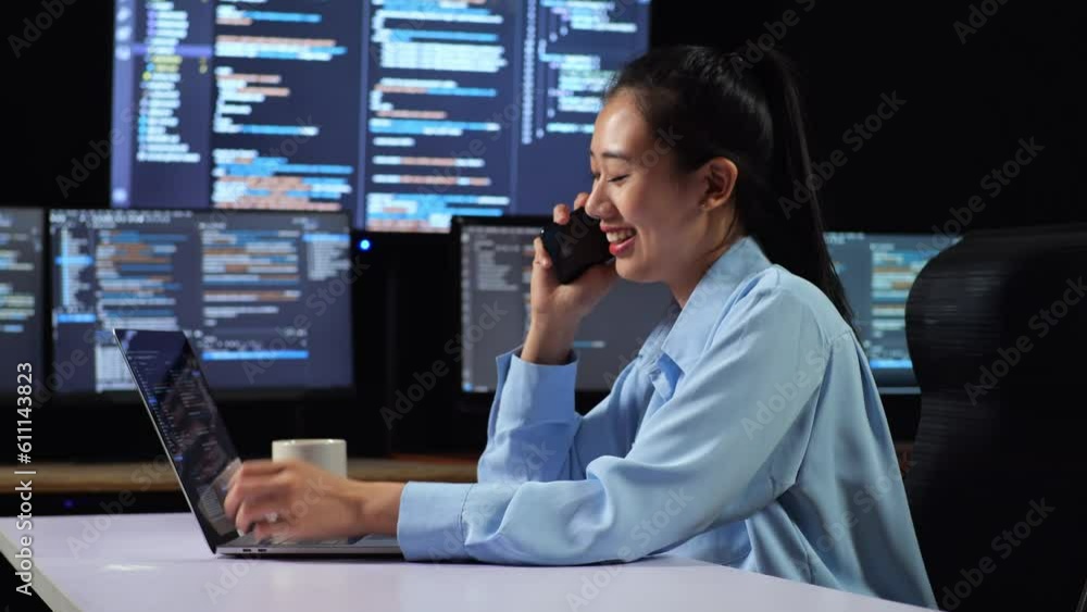 Side View Of Asian Female Programmer Talking On Smartphone While Writing Code By A Laptop Using ...