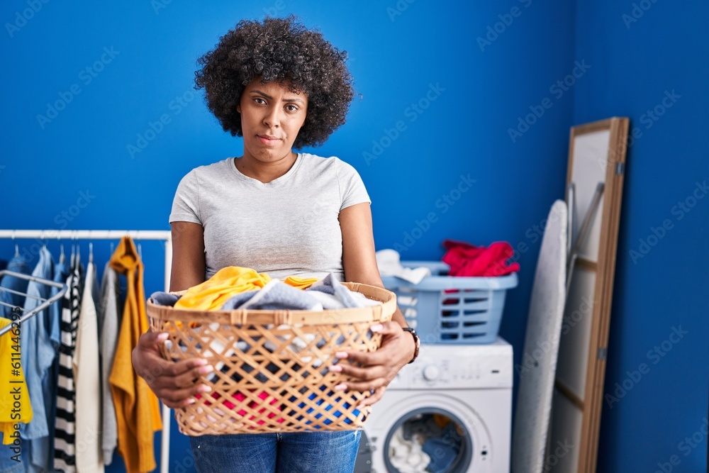 Black woman with curly hair holding laundry basket depressed and worry for distress, crying ...