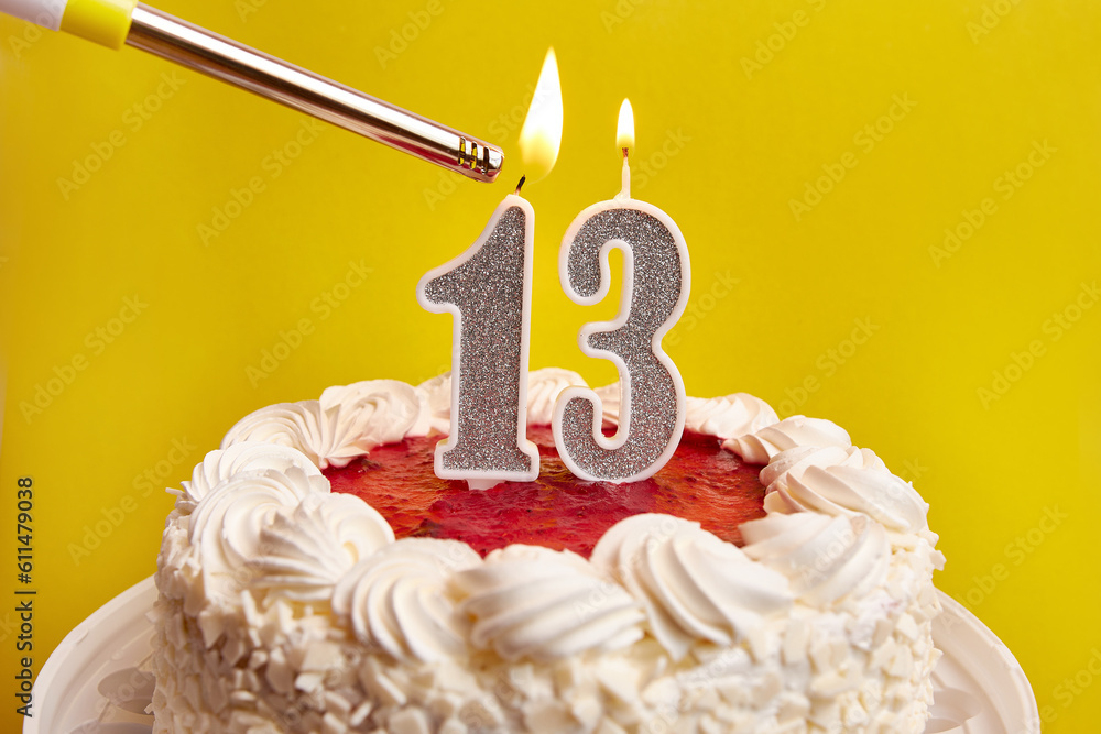A candle in the form of the number 13, stuck in a festive cake, is lit ...