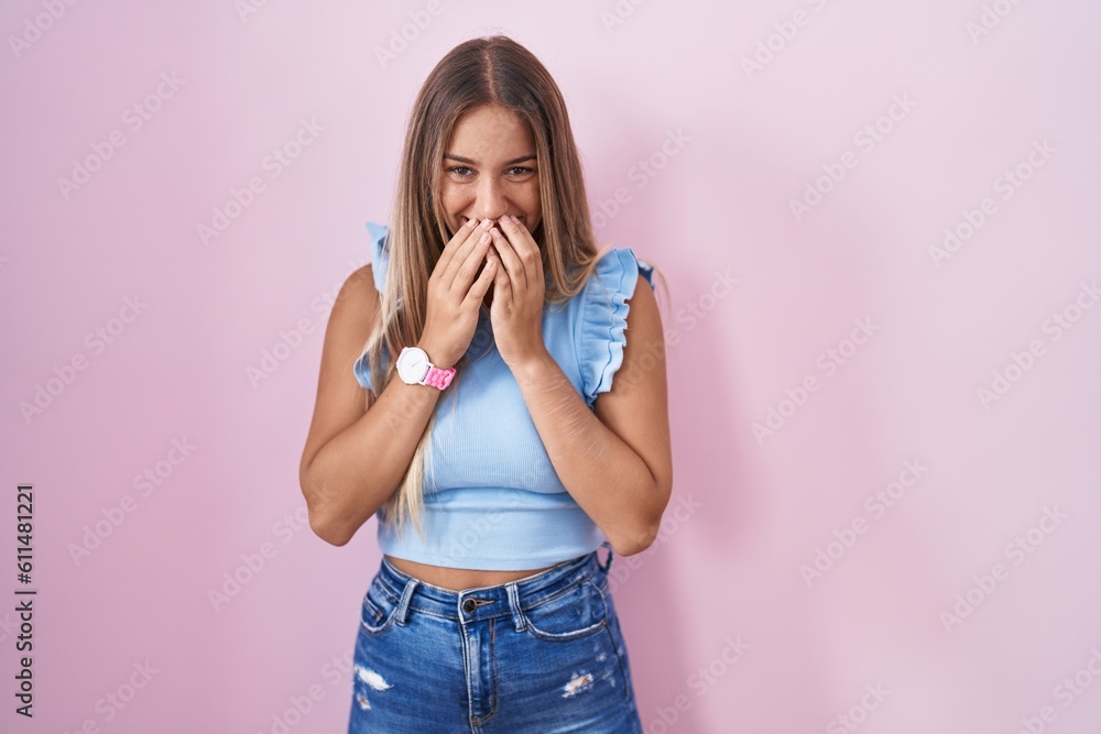 Young blonde woman standing over pink background laughing and ...