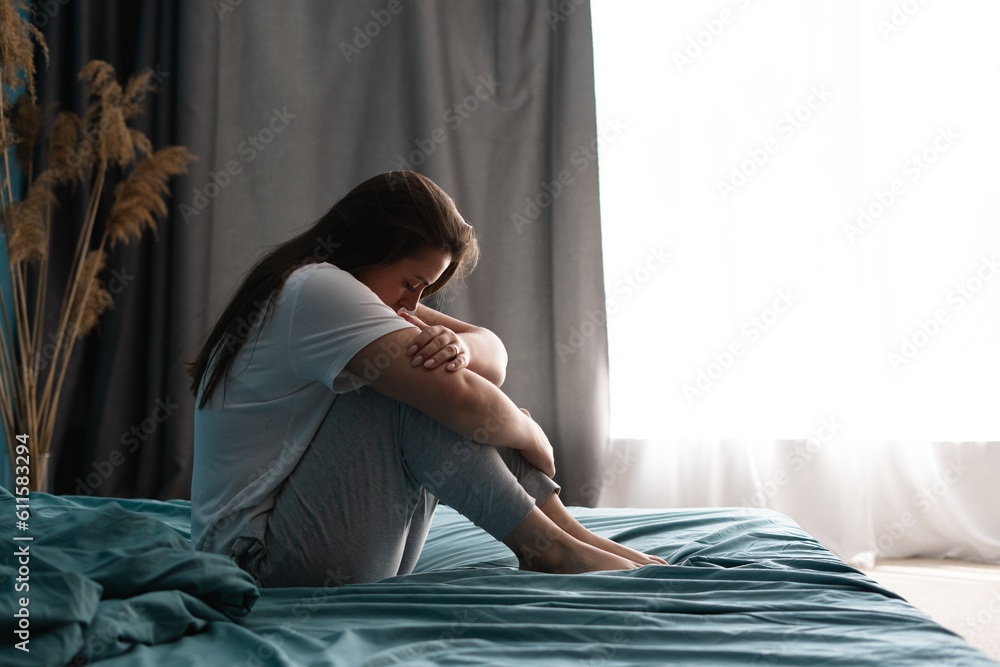 Sad woman sitting on bed in bedroom with light from window. Abuse ...