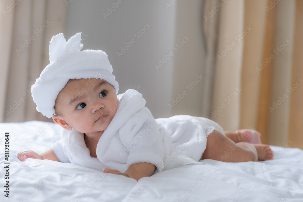 Cute baby girl looking away at back while lay on bed with intense ...