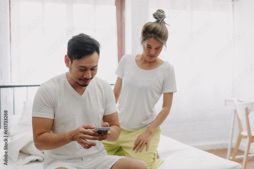 Funny asian couple. Wife peeking husband who chatting on the smartphone. Stock Photo | Adobe Stock