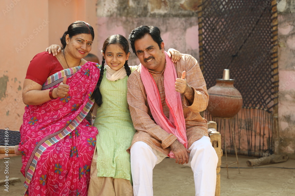 Happy rural Indian family sitting together on a cot outside their ...