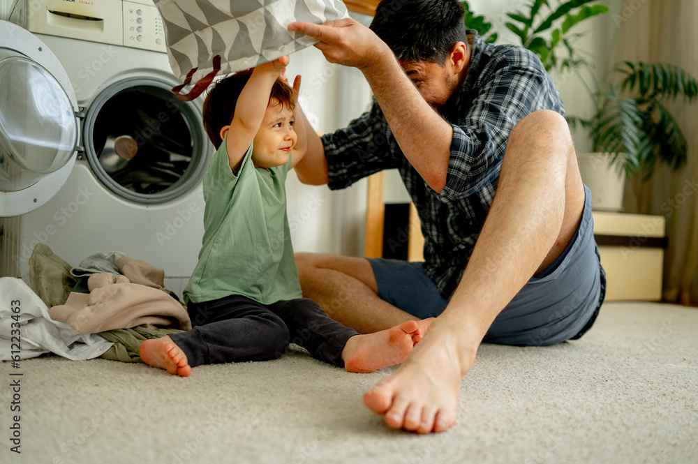 Happy father and son having fun with laundry basket and washing clothes ...