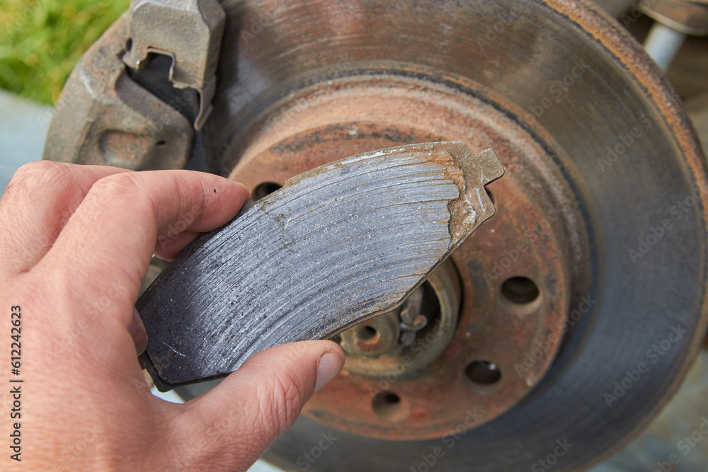car mechanic shows a worn brake pad, a worn brake shoe and a against ...