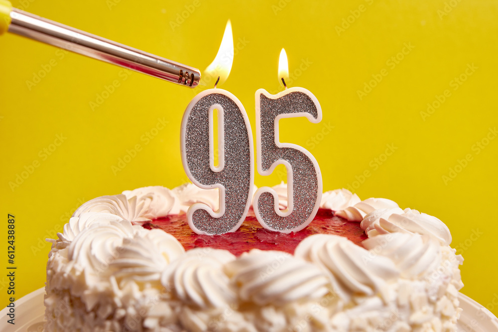 A candle in the form of the number 95, stuck in a festive cake, is lit ...