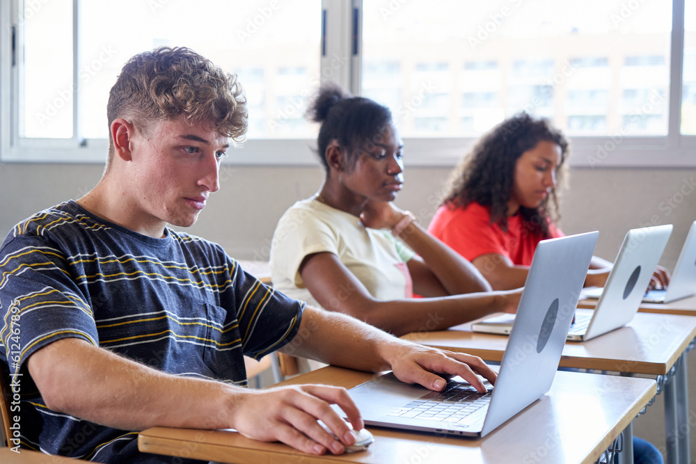 Side view of multiracial teenage students in a classroom studying with ...