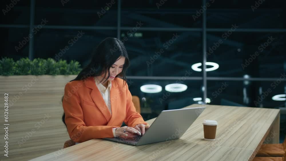 Smiling Korean lady boss working overtime on project in modern loft ...
