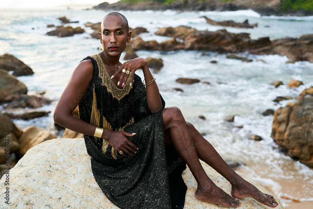 Androgynous ethnic fashion model in luxury dress, jewelry sits on rocks ...