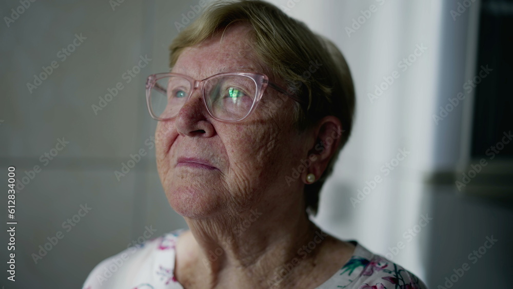 Contemplative elderly senior woman in 80s standing by window looking ...