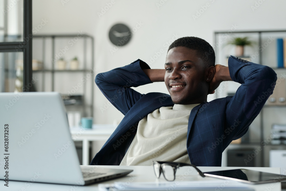 Young restful businessman keeping hands behind head and looking at ...