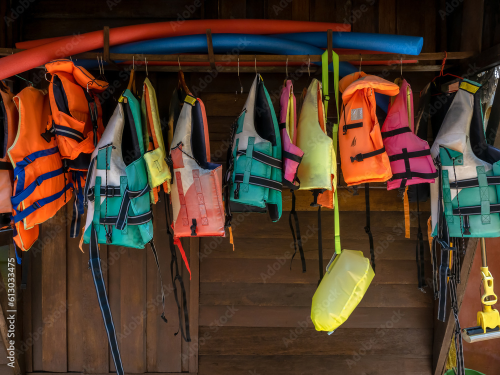 Multi-colored life jacket vests are hung on rail on wood wall for ...