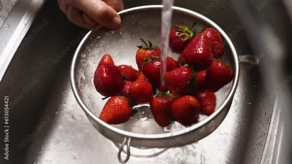 Strawberries in a sieve are washed with a splash of water. Close-up ...