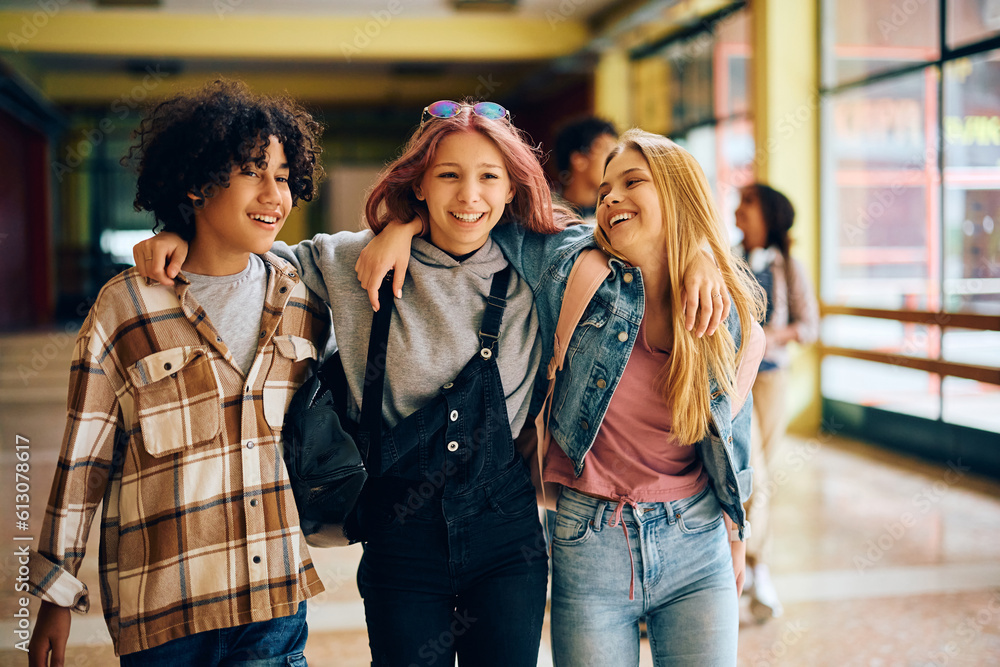 Happy high school friends walk embraced through hallway at school ...